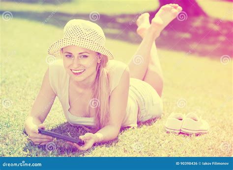 Woman Lying On Green Grass In Park And Holding Mobile Phone In H Stock