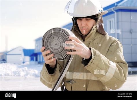 A Firefighter In Full Gear Carefully Inspects A Rolled Fire Hose During