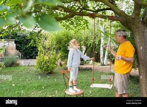 Granddaughter Helping Grandfather Making Swing With Rope In Garden