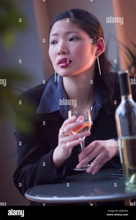 Attractive Asian Woman Sitting Alone At A Café Table With A Glass Of