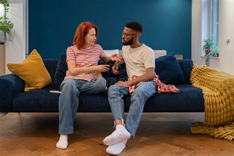 Unhappy Young Diverse Married Couple Sitting On Sofa Talking About