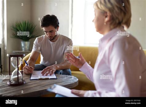 Attentive Young Man Listening To Female Counselor And Drawing On