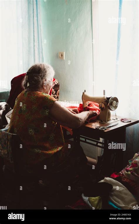 An Old Plump Gray Haired Woman With Curly Hair Sews On A Vintage Retro