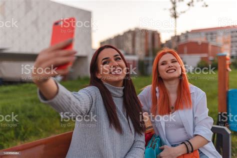 Two Redheaded Women Taking Selfies While Sitting On A Park Bench