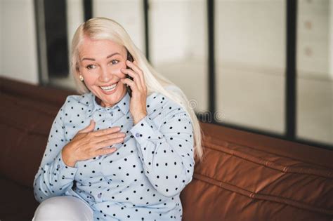 Blonde Mature Woman Talking On The Phone While Sitting On The Sofa