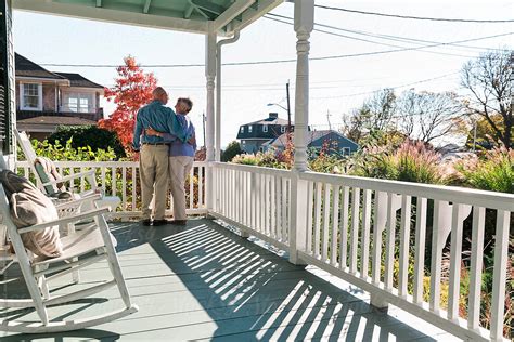 Senior Couple On Porch Of Home Arm In Arm Hugging Together By Stocksy