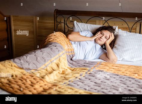 Sad Curly Brunette Woman Lying On Bed Under Terry Covers With Worried