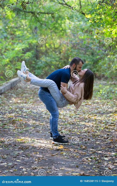Young Beautiful Couple In The Park A Man Holds A Woman In His Arms In