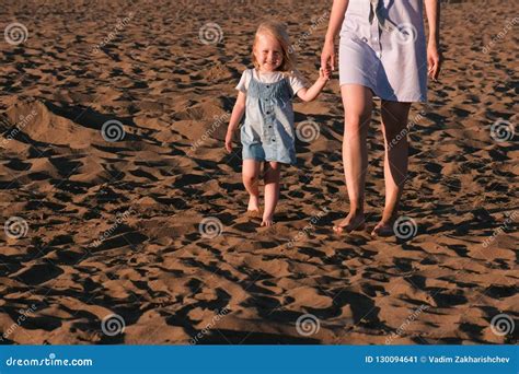 Beautiful Blonde Mom And Daughter Walk On The Beach At Sunset Stock