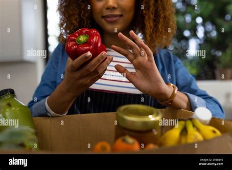 Happy Biracial Woman Unpacking Grocery Shopping From Box In Kitchen