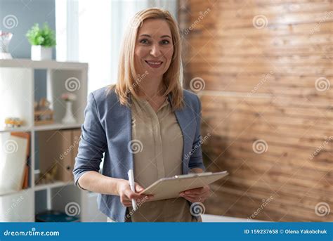 Waist Up Of Smiling Female Psychologist Holding Clipboard And Pen In