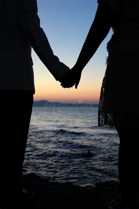 Romantic Silhouette Couple Holding Hands On A Beach In Sunset Stock