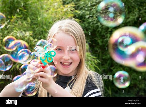 Ten Year Old Blonde Girl Uses A Small Machine To Blow Bubbles At The