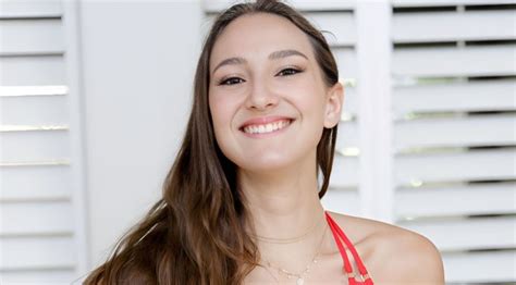 A Woman With Long Brown Hair Wearing A Red Halter Top Smiling At The Camera