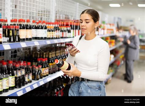 Young Girl Scanning Barcode On Bottle Of Soy Sauce With Phone At Asian