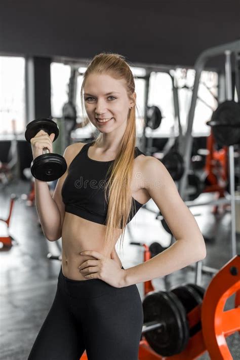 Young Woman In Black Top Doing Exercises With Dumbbells At The Gym