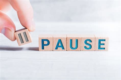 the word pause formed by wooden blocks and arranged by male fingers on