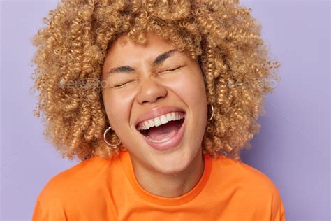 Close Up Shot Of Overjoyed Curly Haired Woman Exclaims Loudly Keeps