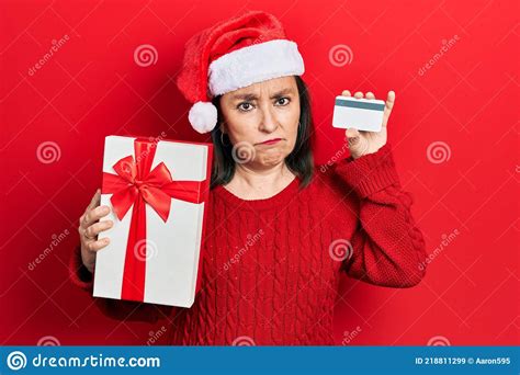 Middle Age Hispanic Woman Wearing Christmas Hat Holding T And Credit