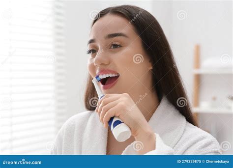 Young Woman Brushing Her Teeth With Electric Toothbrush In Bathroom