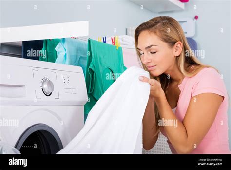 Woman Smelling Clean Clothes Near The Electronic Washer At Laundry Room