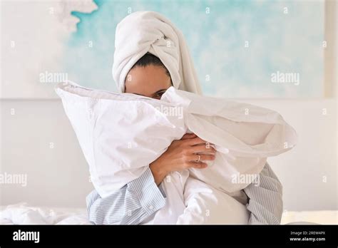 Female With Towel On Head Hiding Face Behind White Pillows While