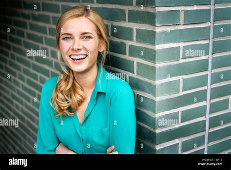 Portrait Of A Cheerful Young Woman Leaning Against Wall With Arms