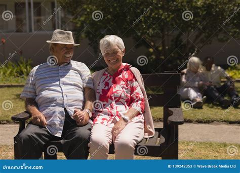 Front View Of Senior Couple Holding Hands And Sitting On Bench In