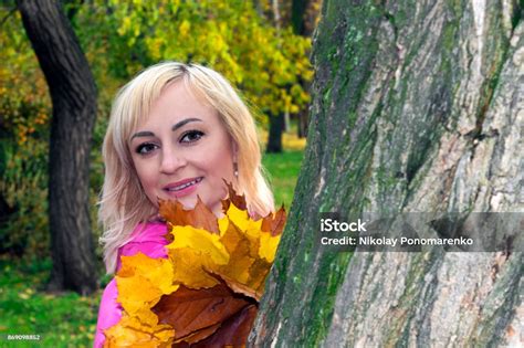 Beautiful Girl Peeks From Behind A Tree With A Bouquet Of Maple Leaves