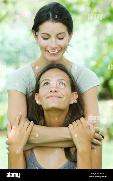 Mother Embracing Teen Daughter From Behind Both Smiling At Each Other