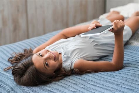 Muchacha Sonriente Que Miente En La Cama Que Sostiene La Tableta