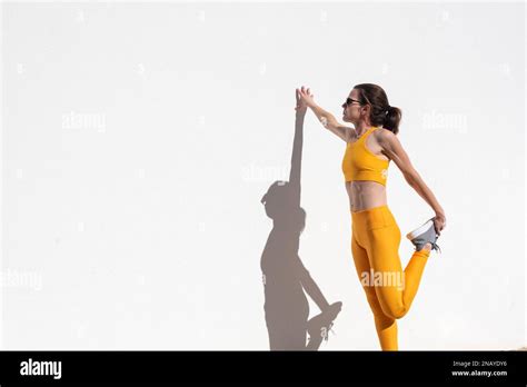 Sporty Woman Doing A Leg Stretch Warm Up Exercise Against A White Wall