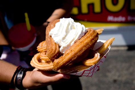 A Person Holding Up A Cupcake With Whipped Cream On Top And Pretzels In