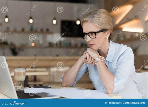 Serious Mature Businesswoman In Eyeglasses Using Laptop While Working