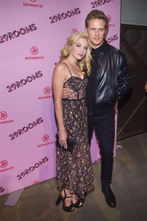 A Man And Woman Standing Next To Each Other In Front Of A Pink Wall