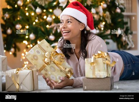 Happy Biracial Woman In Santa Hat Lying Under Christmas Tree Stock