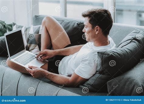 Man In Underwear Lying On The Sofa And Using Modern Laptop Stock Image