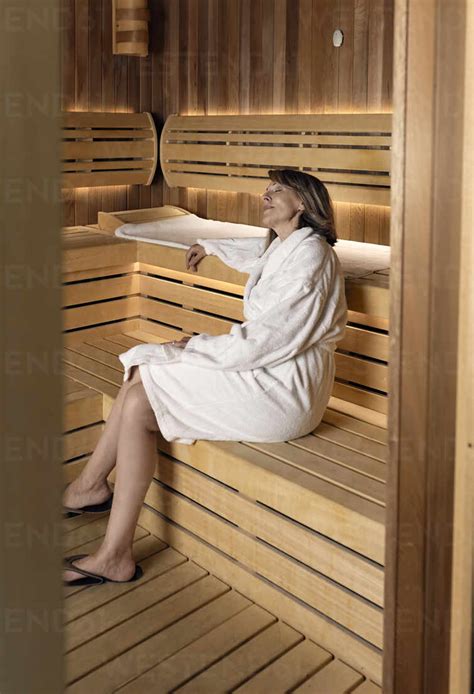 Thoughtful Woman Wearing Bathrobe Sitting On Wooden Sauna At Health Spa