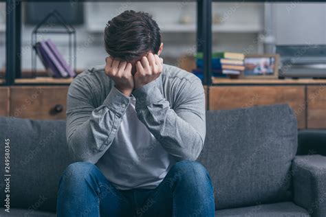 Man Sitting On Couch Crying And And Covering Face With Hands At Home
