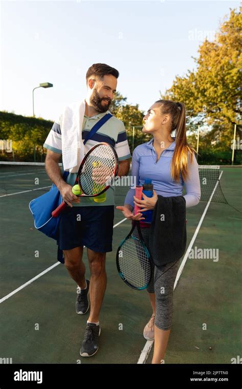 Happy Caucasian Couple Holding Rackets And Water Bottles Talking On