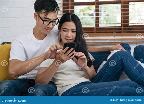 Asian Young Couple Are Looking At A Smartphone In Their House Happy
