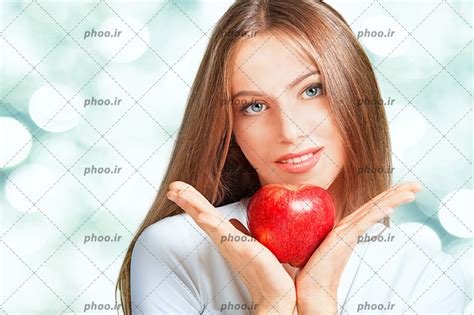 عکس با کیفیت خانم زیبا با چشم های آبی و مو های قهوه ای که یک سیب قرمز