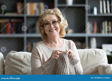 Elderly Woman Sit On Couch Holding Knitting Needles And Yarn Stock