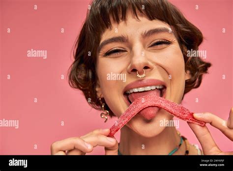 Happy And Young Woman With Nose Piercing Licking Sweet And Sour Candy