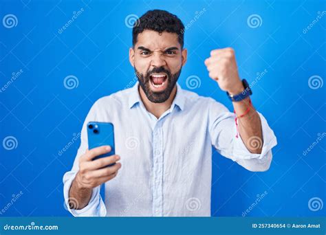 Hispanic Man With Beard Using Smartphone Typing Message Angry And Mad