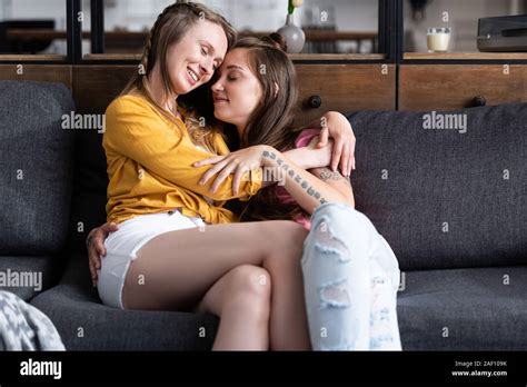 Two Pretty Lesbians Embracing While Sitting On Sofa In Living Room
