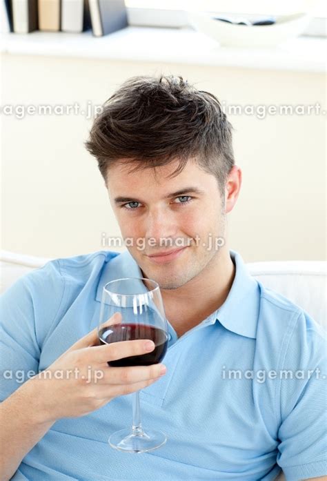 Handsome Young Man Sitting On A Sofa Holding Wineglass In The Living