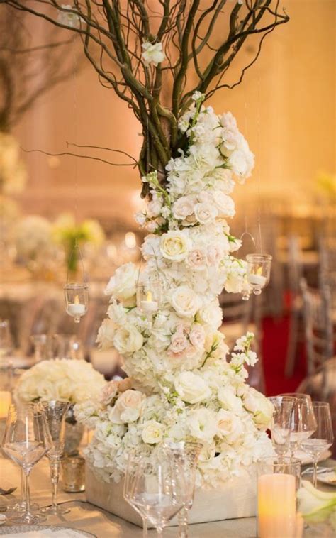 A Tall Centerpiece With White Flowers And Greenery
