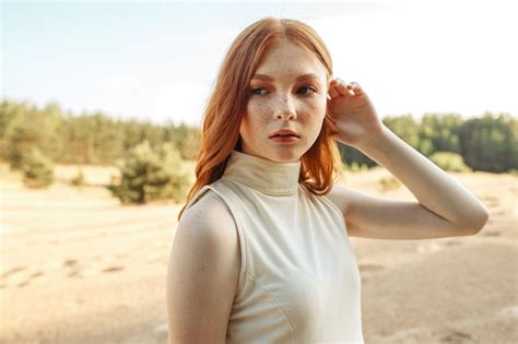 Portrait Of Young Woman With Freckles Touching Long Wavy Ginger Hair