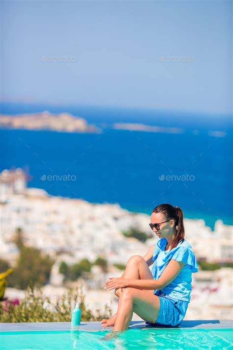 Slim Woman Applying Sunscreen On Her Legs Sitting On The Edge Of Pool